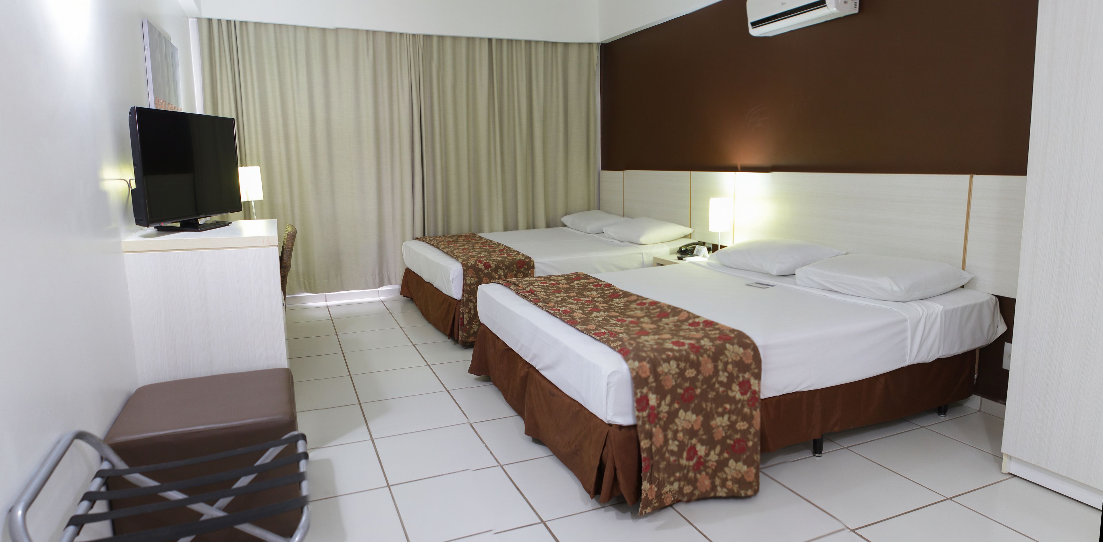 Quarto de hotel com duas camas, televisão, secretária e uma cadeira.