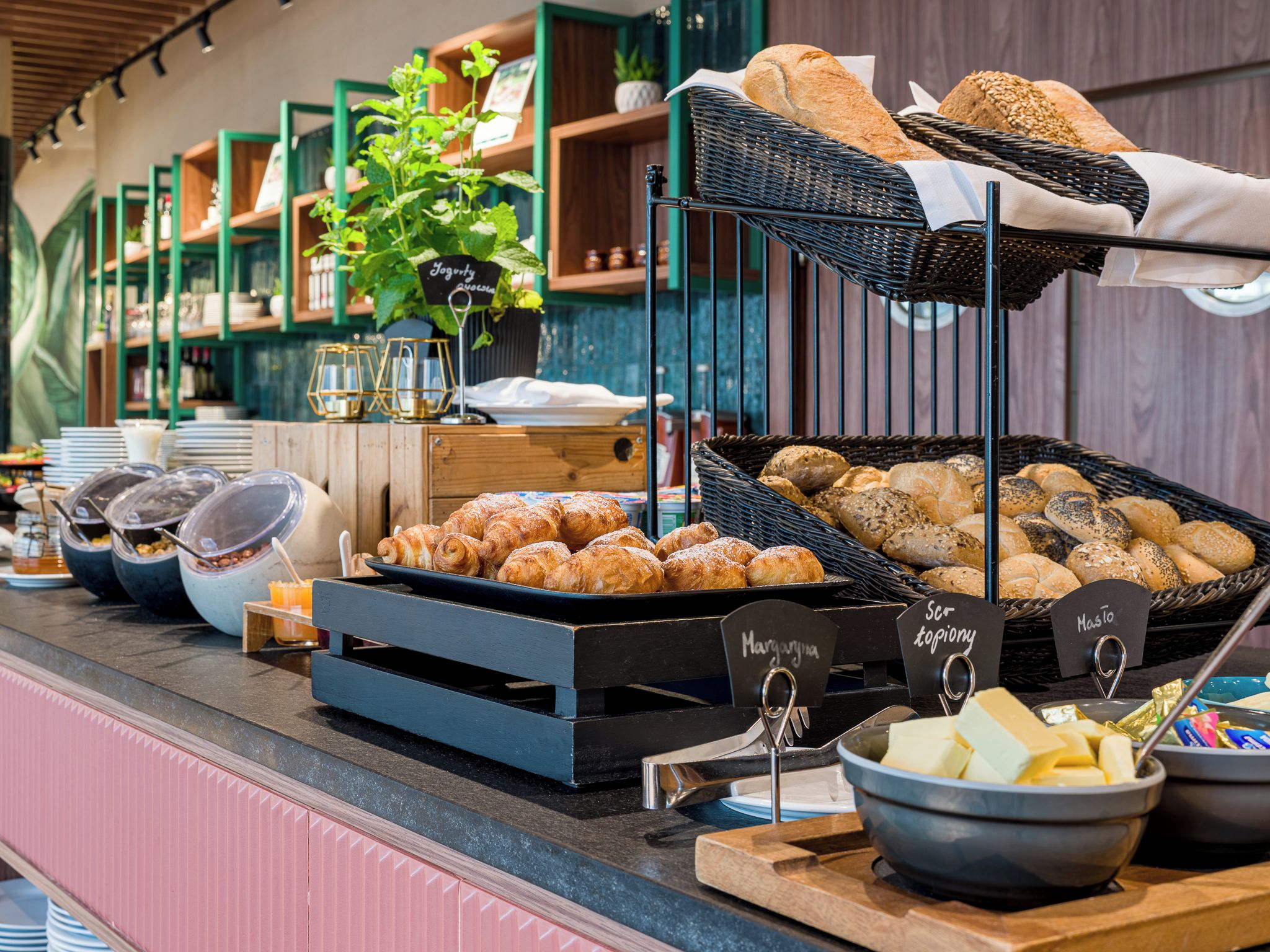 Buffet com diversos produtos de panificação, incluindo croissants e pão, e seções identificadas para diferentes tipos de queijo.