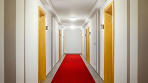 Um corredor longo com carpete vermelho, portas de madeira e paredes brancas.