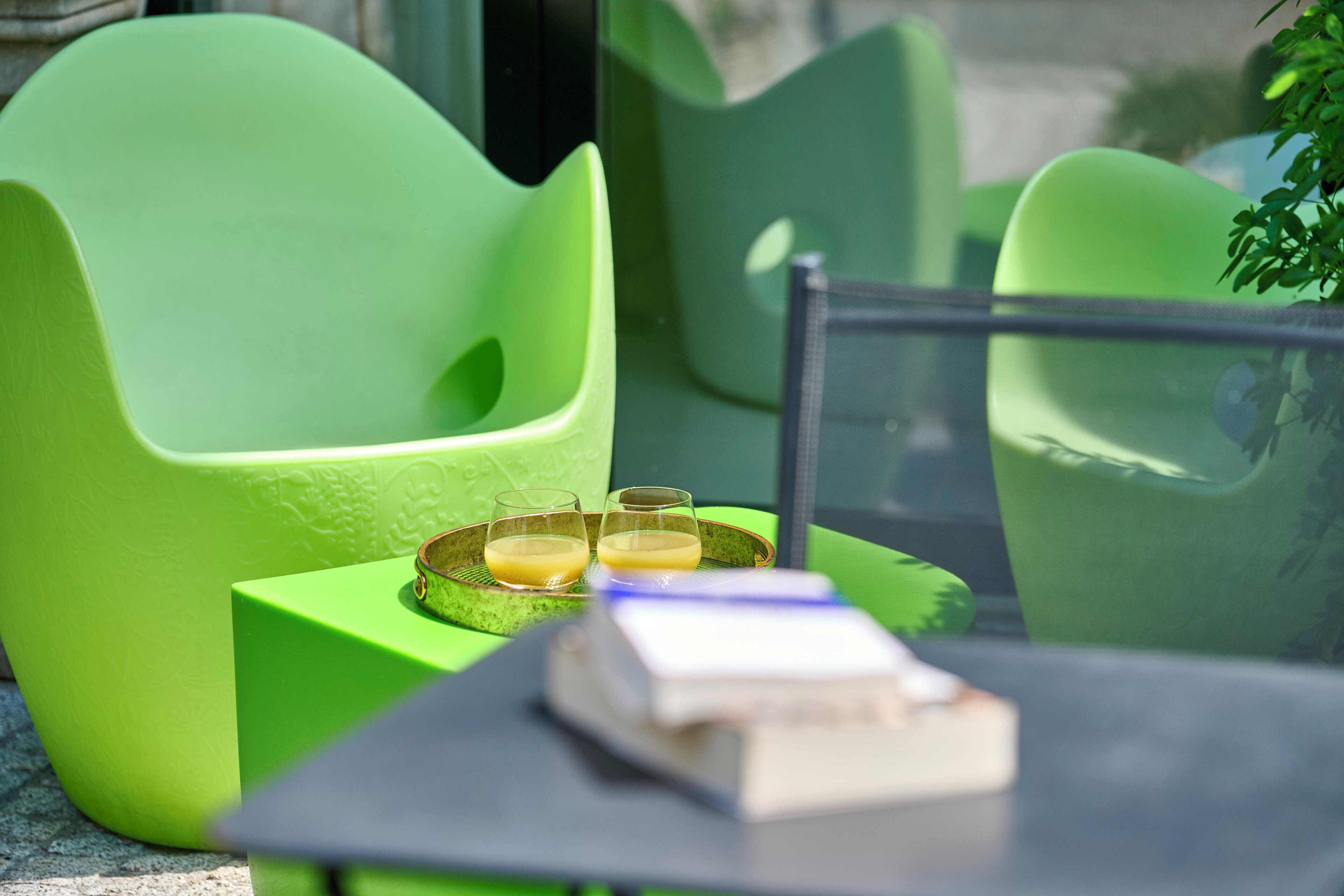 Uma área de estar com cadeiras verdes e uma mesa com um livro e dois copos de suco de laranja.