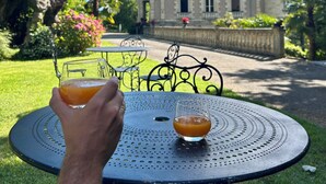 Uma mesa com dois copos de suco de laranja num jardim com um grande edifício de pedra ao fundo.