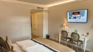 Quarto de hotel com cama, escrivaninha e televisão exibindo um programa.