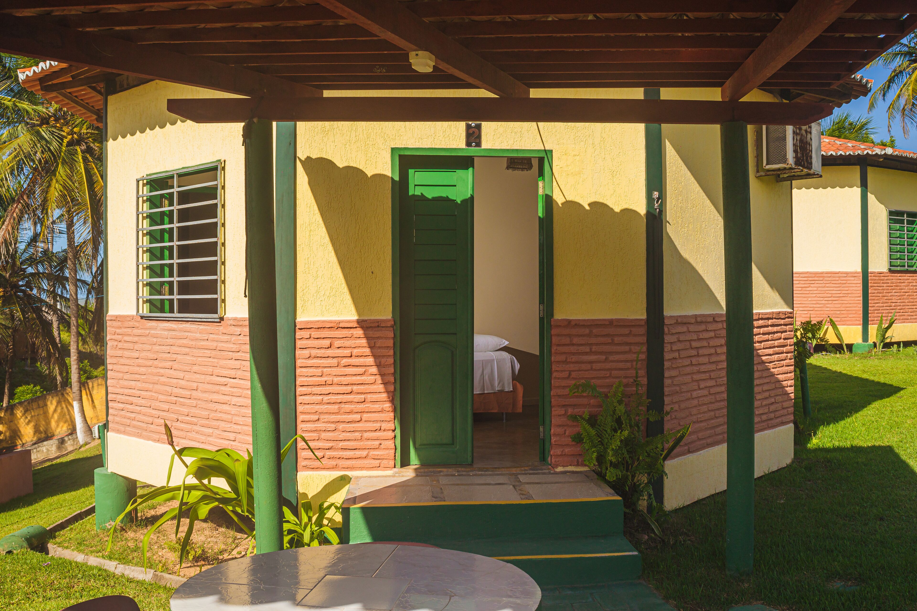 Um edifício com porta verde, janela com grades e uma cama pequena no interior.