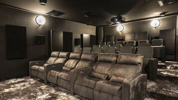 Sala de cinema com um amplo sofá seccional cinza escuro, várias fileiras de assentos e projetor montado no teto.