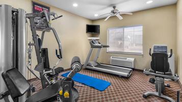 Centro de fitness com equipamentos de cardio, televisão e ventoinha no teto.