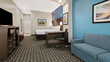 Quarto de hotel com cama, escrivaninha, cadeira, sofá, televisão e tapete estampado.