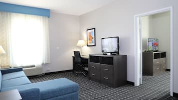 Quarto de hotel com um sofá azul, uma escrivaninha com cadeira, uma televisão e um guarda-roupa.