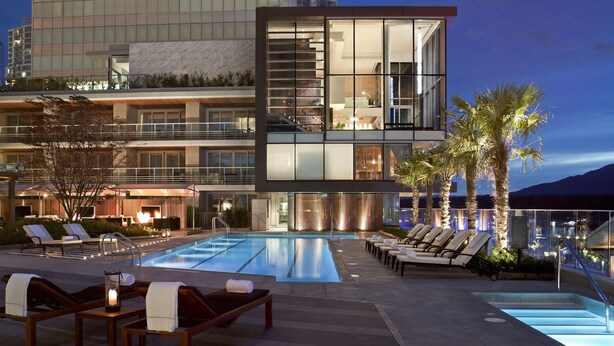 Um hotel moderno com piscina no terraço, espreguiçadeiras e vista para o horizonte da cidade.