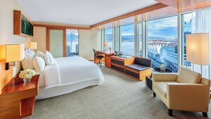 Quarto de hotel moderno com uma cama grande, uma mesa de escritório, um sofá e vista para a paisagem urbana através de amplas janelas.