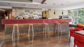 Uma área de bar moderna com balcão vermelho, vários taburetes e uma variedade de garrafas e copos.