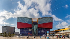 Um edifício moderno com fachada de vidro ampla e uma escultura de golfinho imponente no centro.