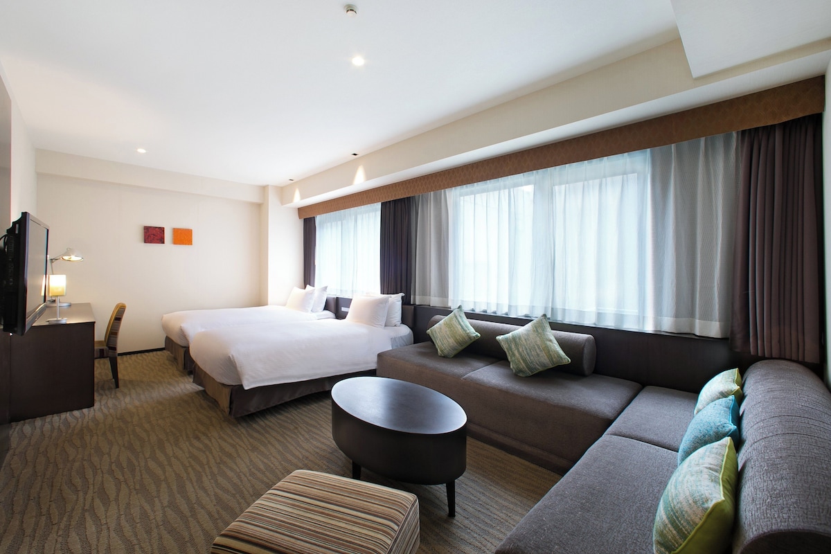 Quarto de hotel com cama, sofá, uma mesinha e escrivaninha com abajur.