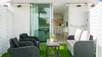 Um pátio moderno ao ar livre com móveis de vime, uma pequena mesa com uma planta e uma porta de vidro deslizante que dá para um espaço interno.