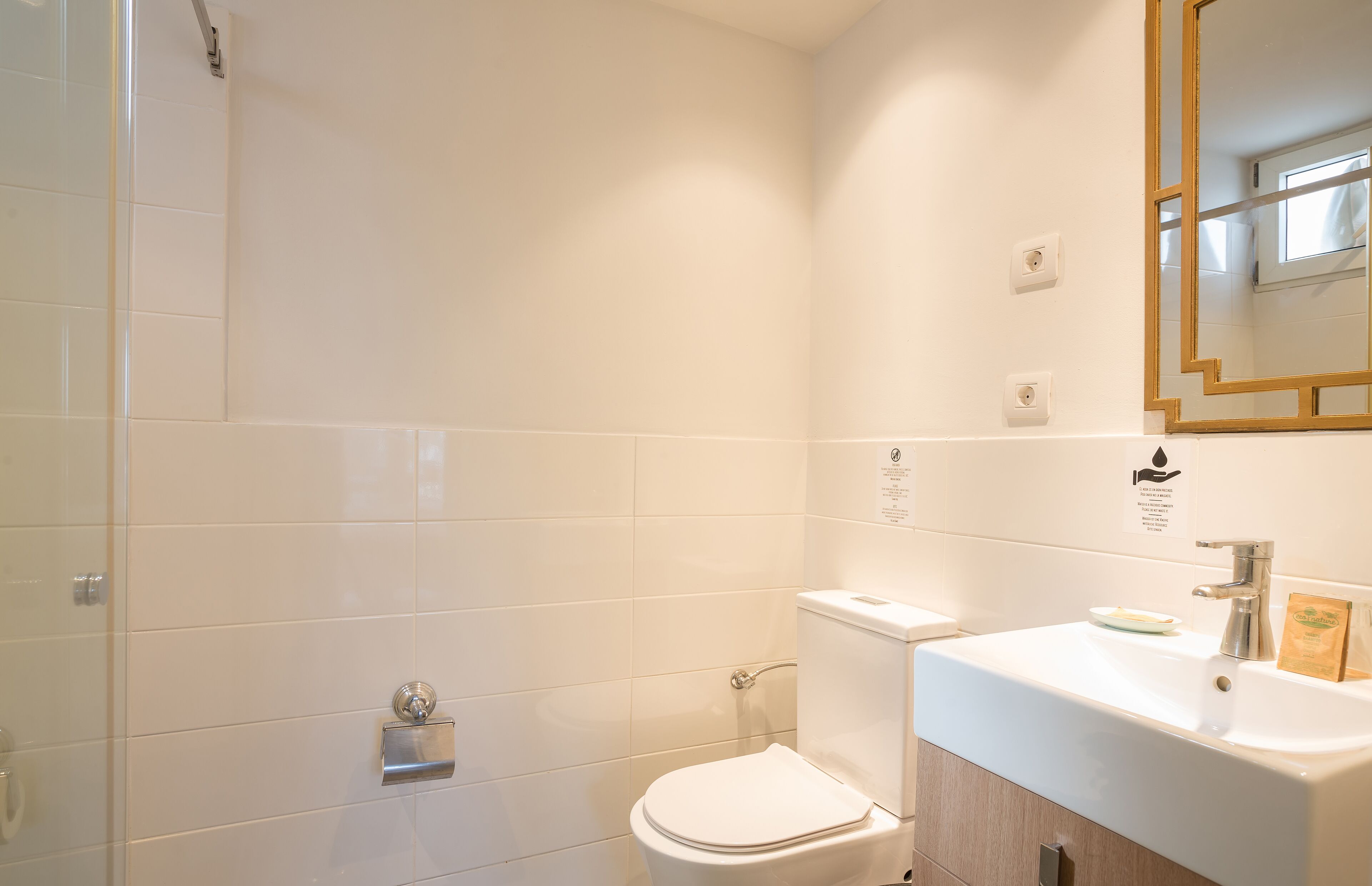 Uma casa de banho moderna com azulejos brancos, sanita, lavatório e espelho.