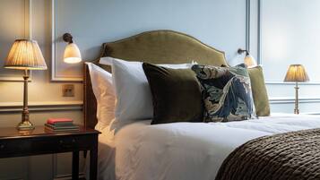 Cama bem arrumada com cabeceira verde, roupa de cama branca e almofadas decorativas. Existem duas luminárias de cabeceira de cada lado da cama.