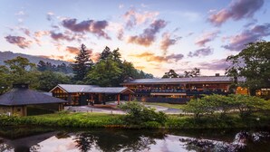 Uma pousada à beira do lago, com um reflexo na água, cabanas de madeira e área de refeições com mesas ao ar livre.
