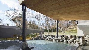 Uma área de piscina moderna ao ar livre, com um pergolado de madeira, degraus de pedra e paisagem natural ao fundo.