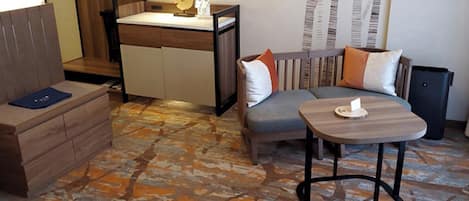 Quarto de hotel moderno com um banco de madeira, uma mesa pequena, um sofá com almofadas e um piso estampado.