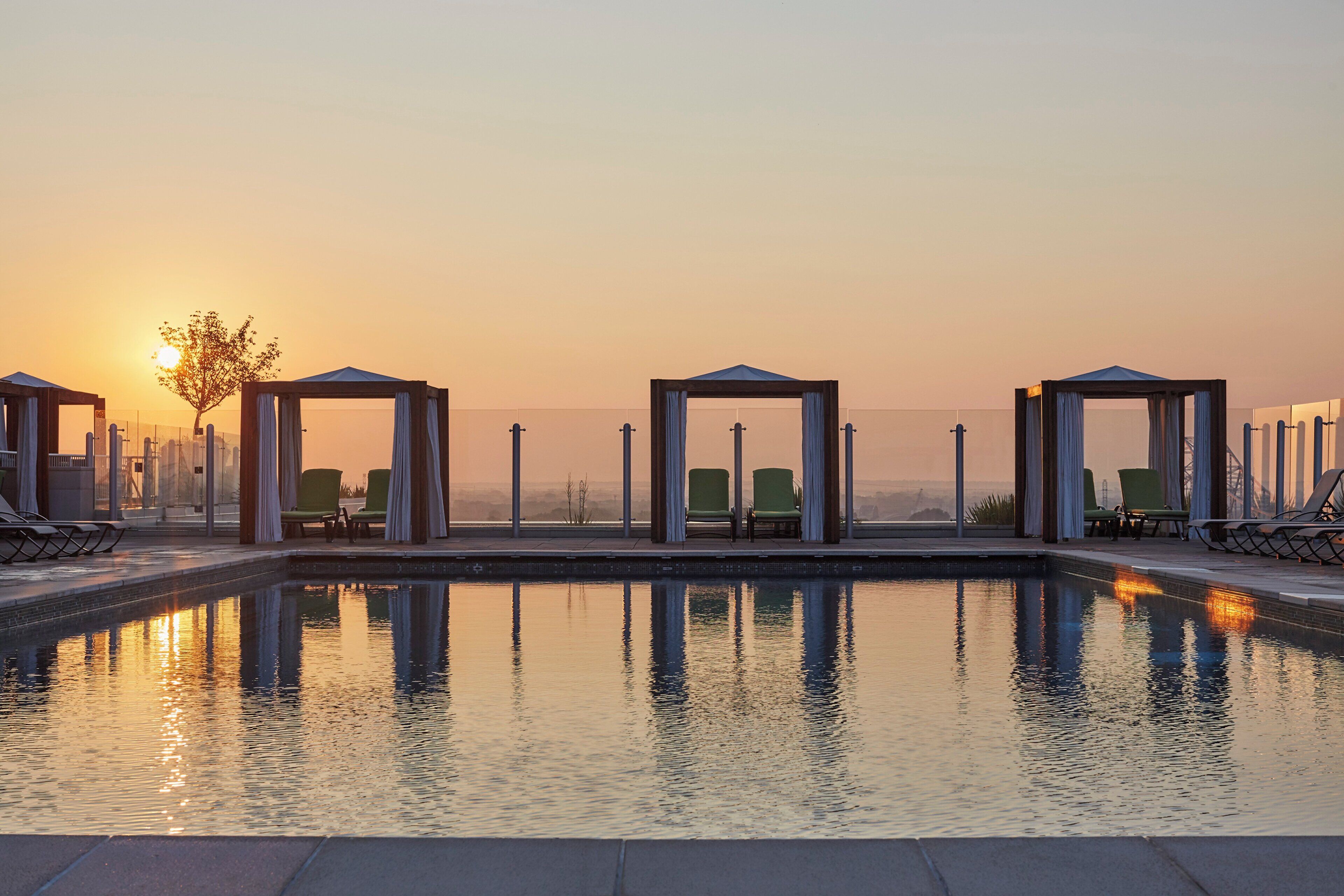 Área à beira da piscina com cadeiras iluminadas pelo sol e vista desobstruída para o pôr do sol.