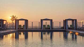 Área à beira da piscina com cadeiras iluminadas pelo sol e vista desobstruída para o pôr do sol.
