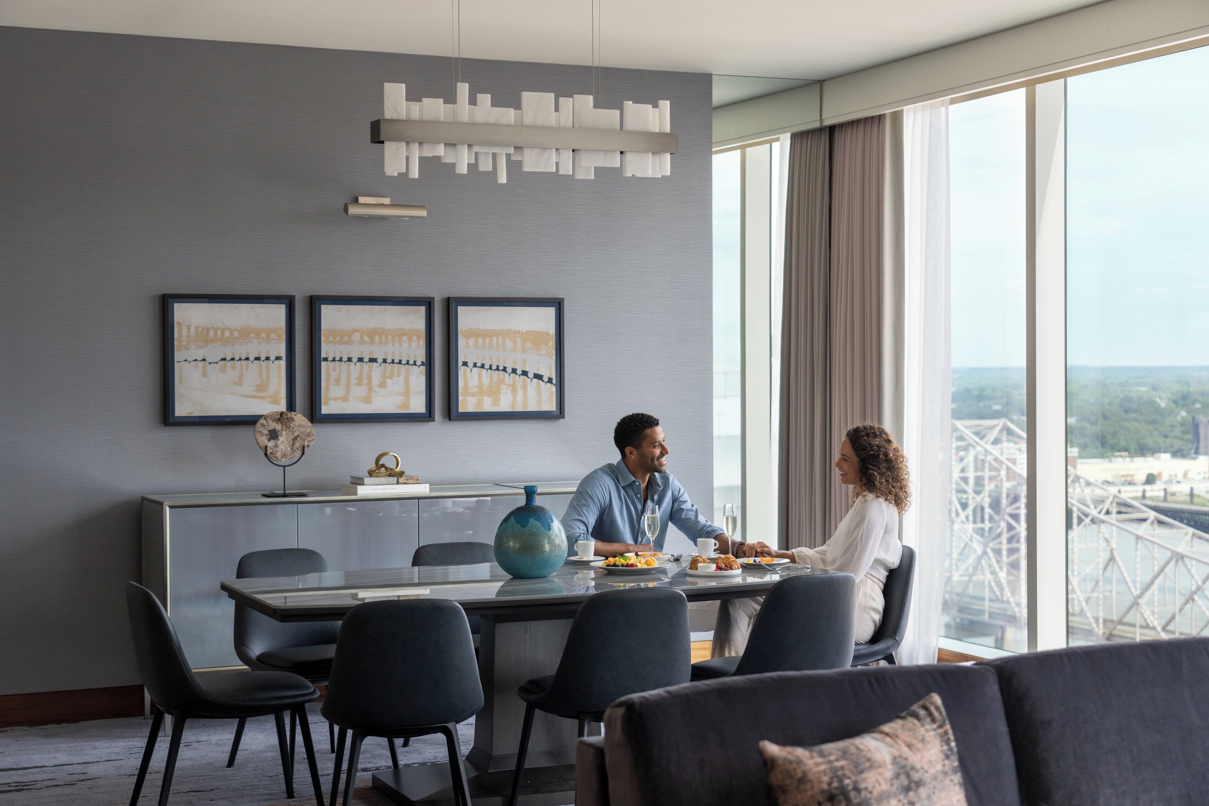 Uma área de jantar moderna com mesa de vidro, cadeiras pretas e quadros na parede.