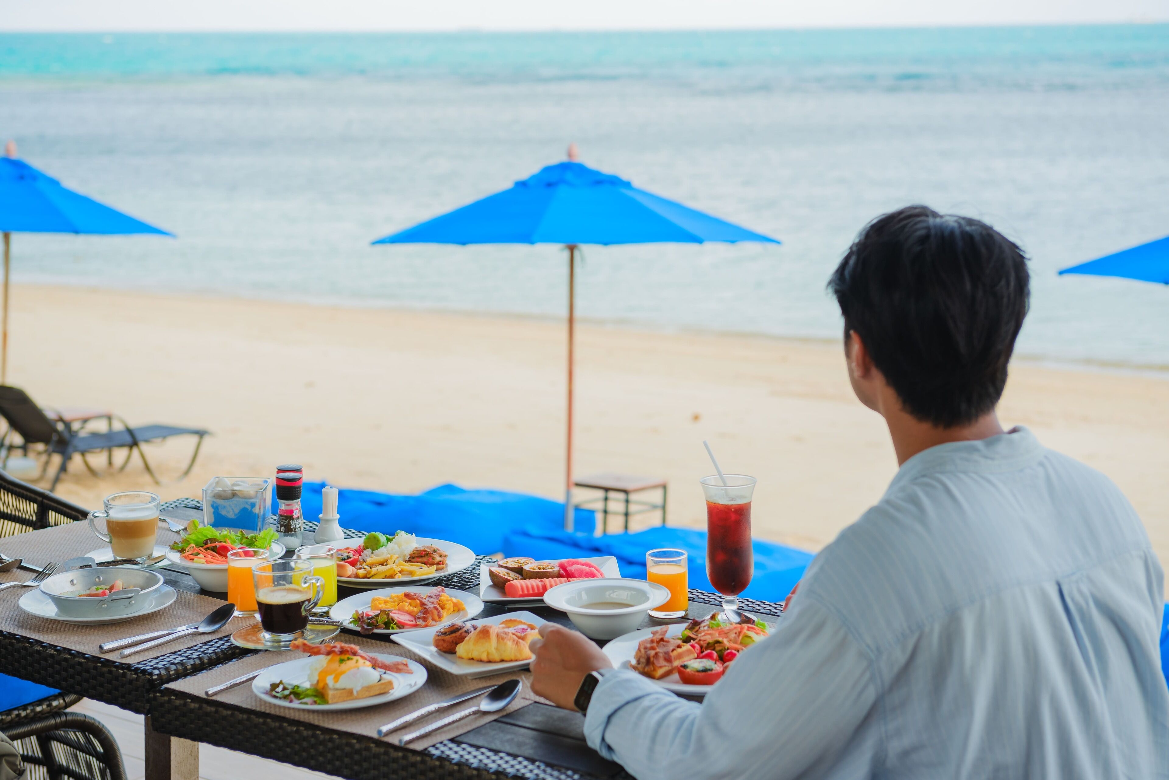 Mesa posta para refeição com diversos pratos e bebidas, com vista para uma praia.