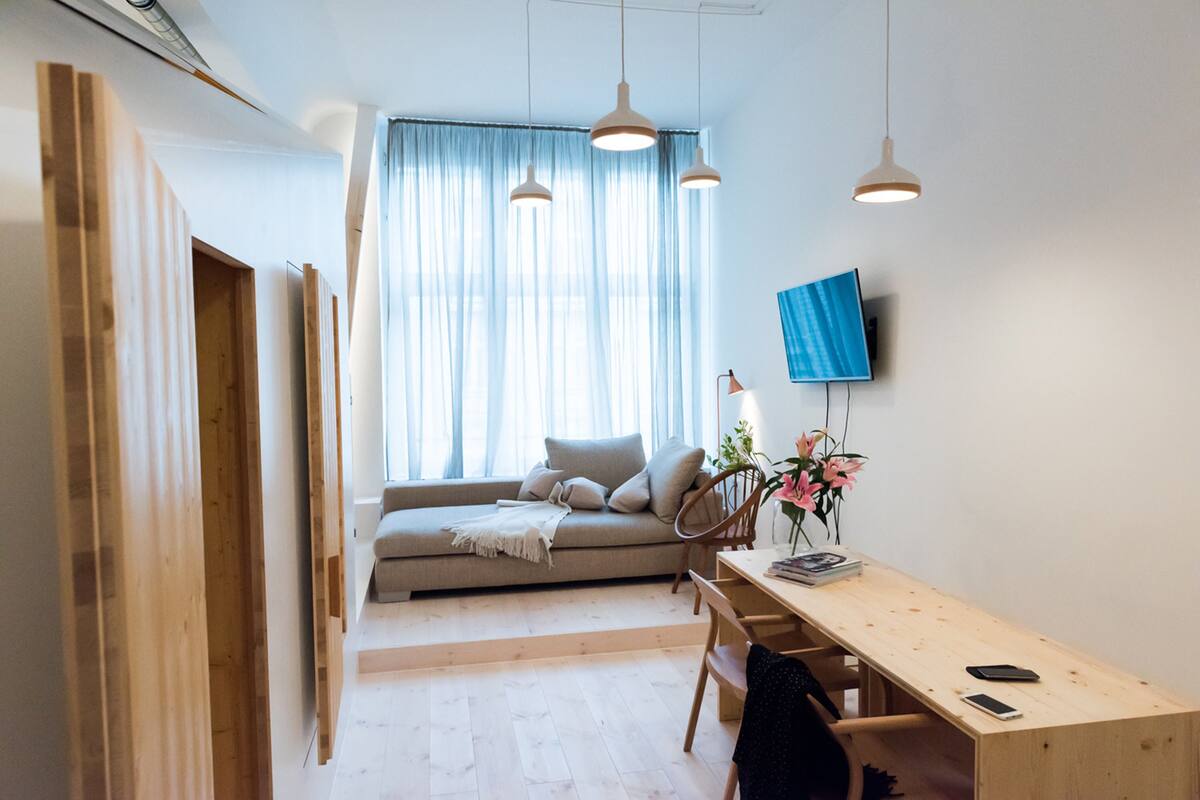 Uma sala de estar moderna com um sofá, uma mesa de jantar de madeira e uma televisão fixada na parede.