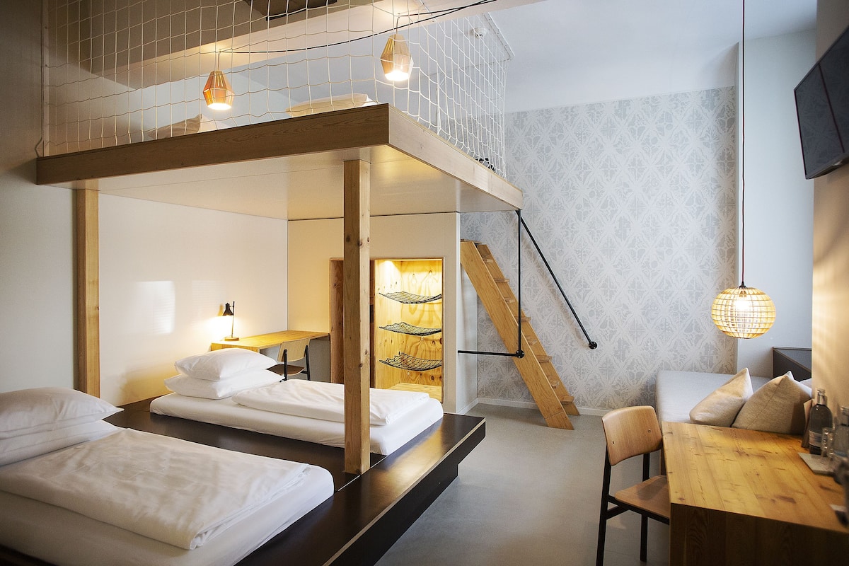 Quarto de hotel moderno com cama beliche, mesa de jantar e escada.