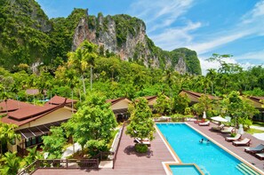 Resort com piscina, deck de madeira e vilas rodeadas por vegetação exuberante e um penhasco.