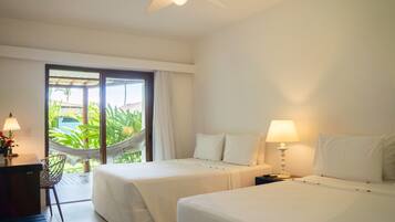 Quarto de hotel com duas camas, uma escrivaninha, uma cadeira, uma rede e vista para o verde lá fora.