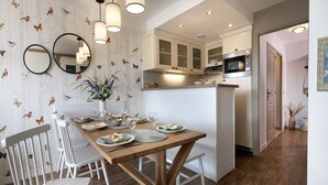 Uma área de refeições com mesa de madeira posta para quatro pessoas, cadeiras brancas e um vaso com flores. Há dois espelhos fixados na parede acima da mesa.