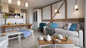 Uma sala de estar moderna com um sofá, uma mesa de jantar e uma área de cozinha ao fundo.