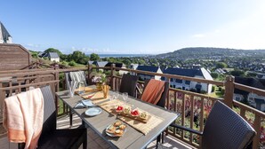 Uma área de refeições com uma mesa posta para dois, com vista para uma paisagem pitoresca de uma cidade e colinas.