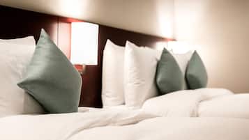 Cama bem arrumada com almofadas brancas e verdes, cabeceira de madeira e luminária fixada na parede.