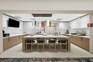Cozinha moderna com ilha central, luminárias pendentes e televisão de tela plana.