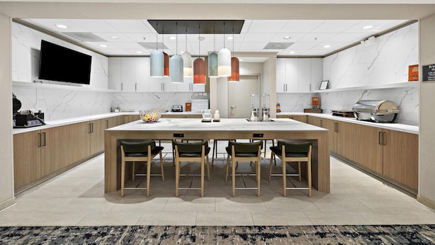 Cozinha moderna com bancada de mármore, armários de madeira e uma ilha central com banquetas.