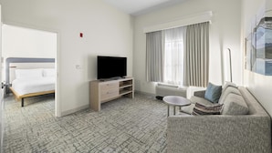 Quarto de hotel com cama, televisão em suporte, sofá e uma pequena mesa.