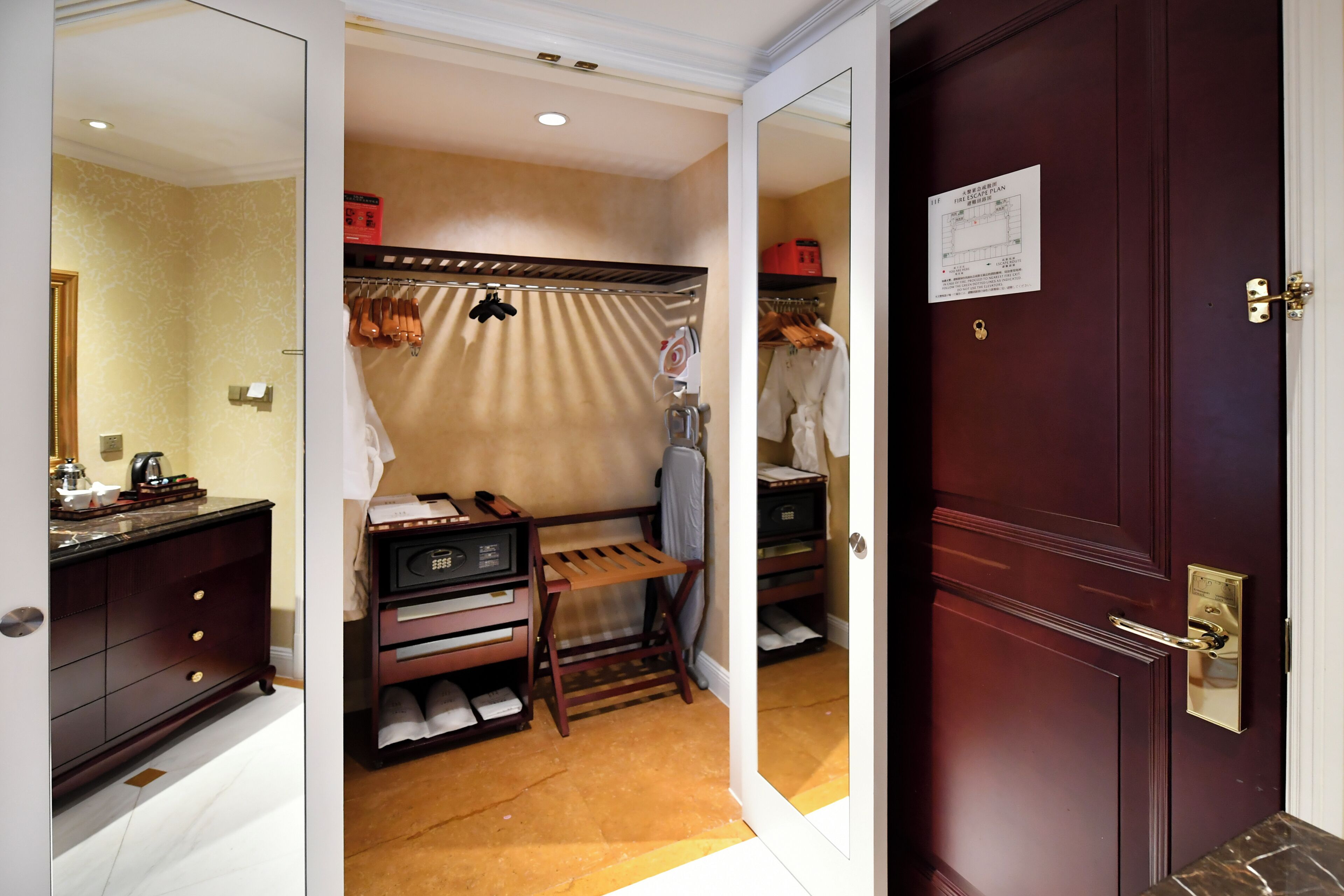 Quarto de hotel com guarda-roupa de madeira, toucador com espelho, cama com cabeceira e porta com tranca.