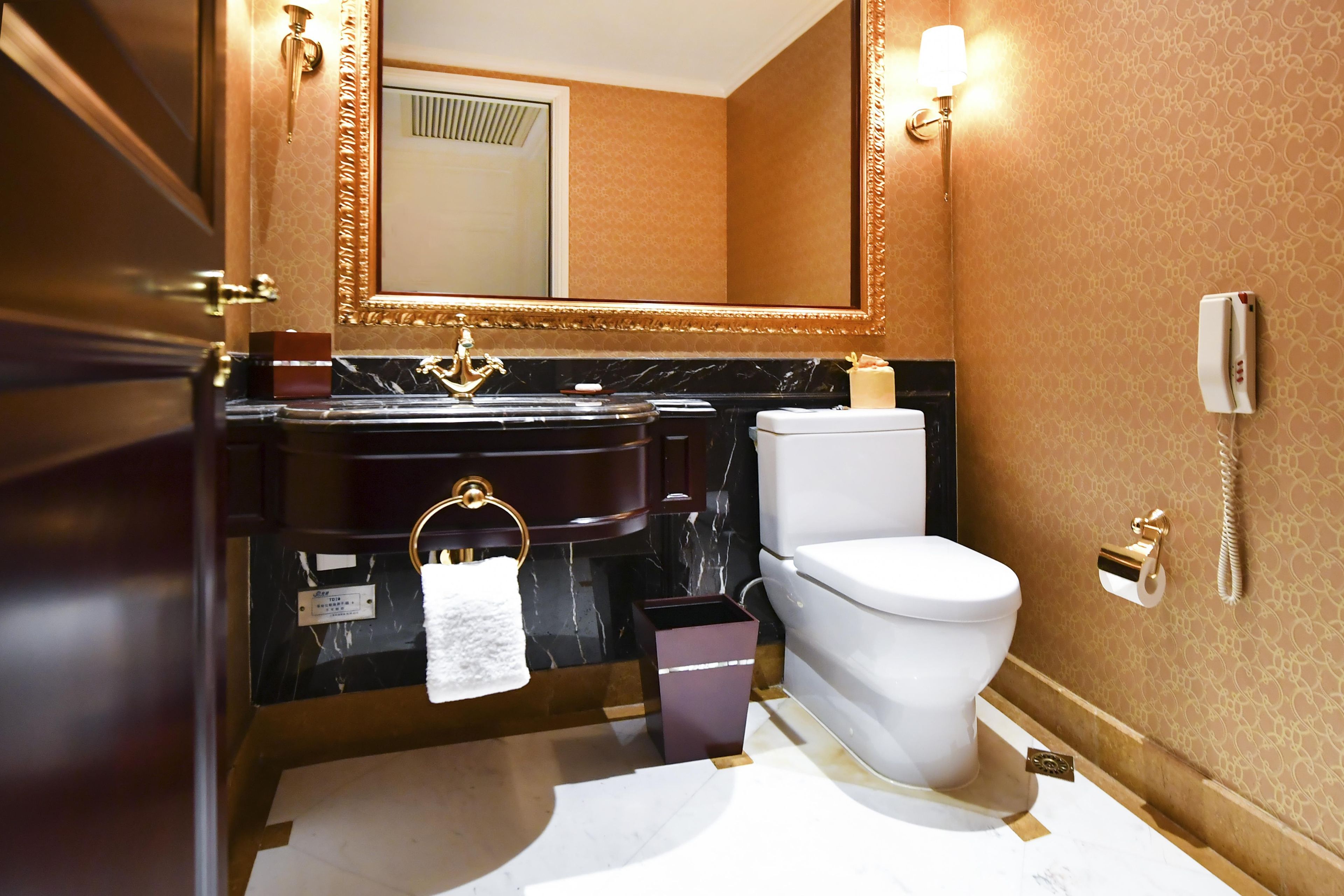 Casa de banho com lavatório de mármore preto, sanita branca e espelho com moldura dourada.