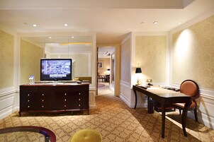 Quarto de hotel com televisão, escrivaninha, cadeira, mesa pequena e sofá.