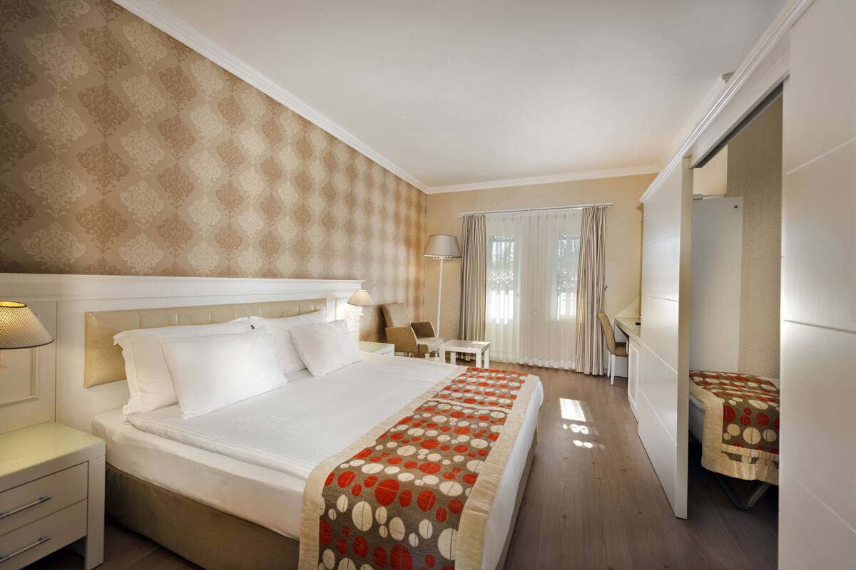 Quarto de hotel com cama grande, escrivaninha, cadeira e guarda-roupa.