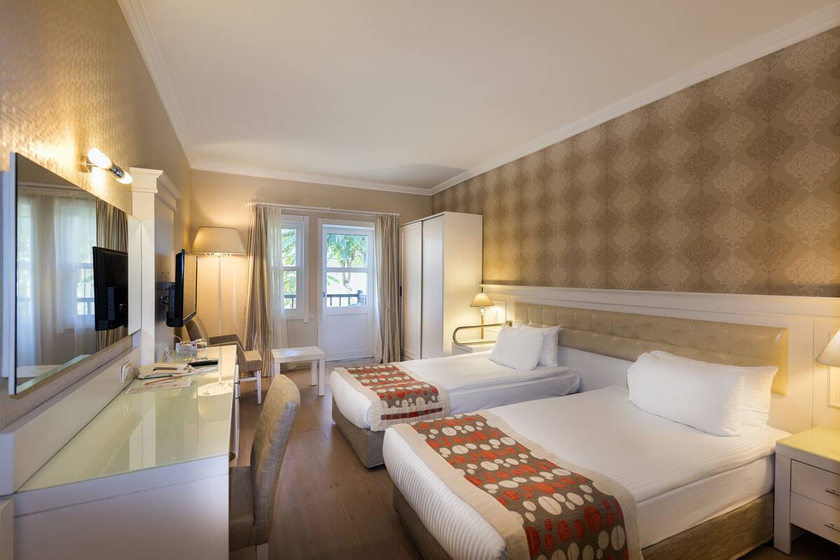 Quarto de hotel com duas camas, televisão, secretária e casa de banho.