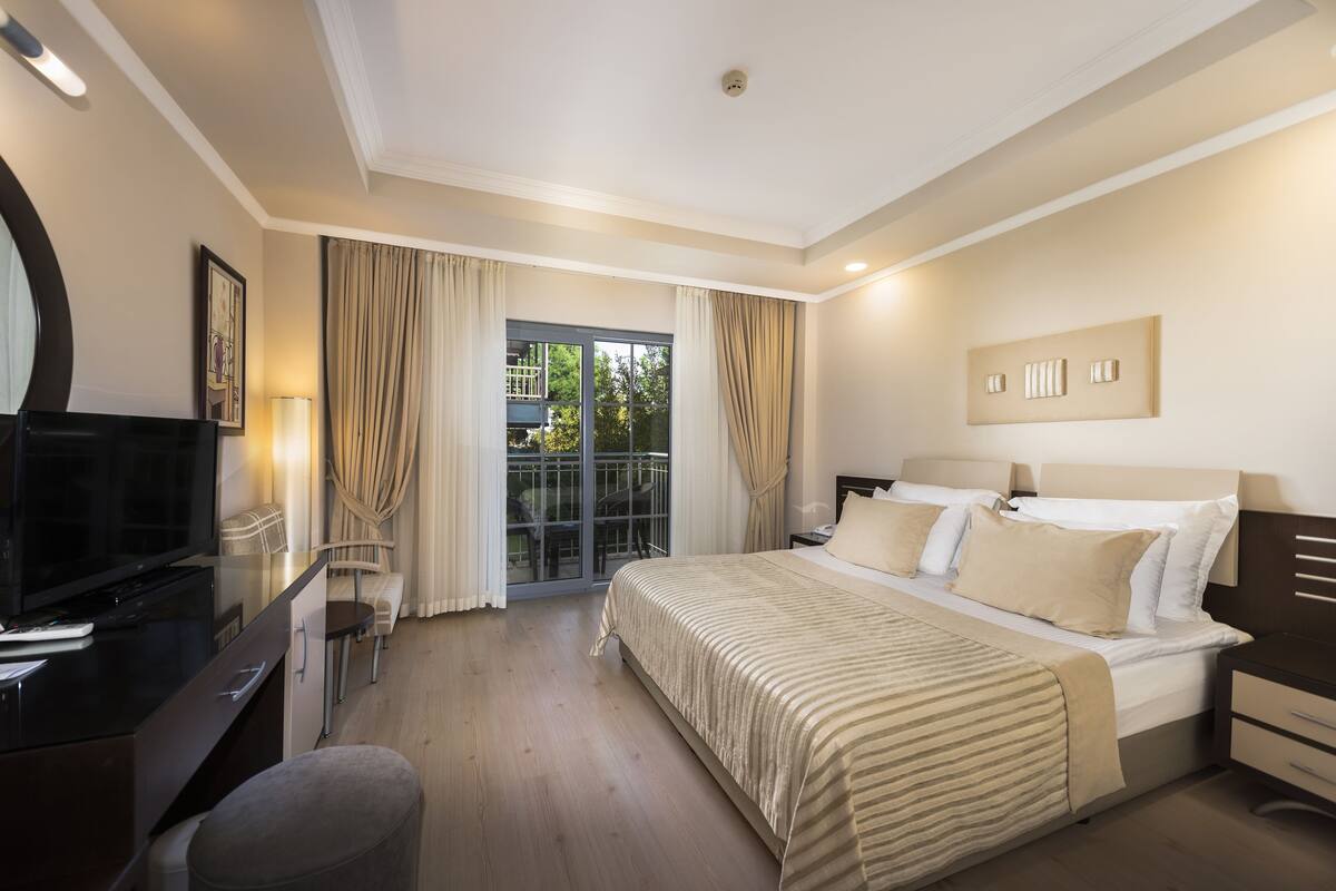 Quarto de hotel com cama, televisão, escrivaninha e cadeira.