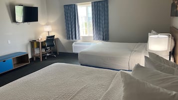 Quarto de hotel com duas camas, uma escrivaninha com cadeira, televisão na parede e janela com cortinas.