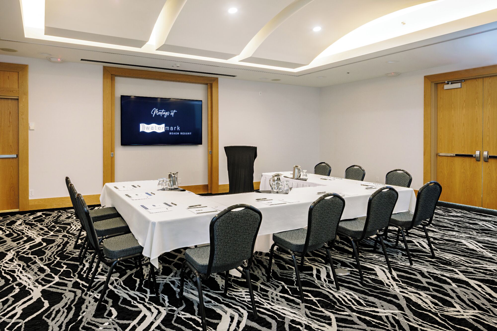 Sala de conferências com uma mesa comprida, cadeiras, tela de projetor e piso coberto de carpete.