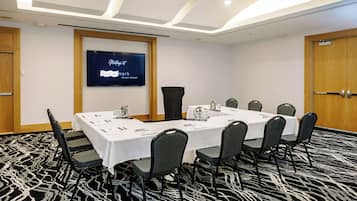 Sala de conferências com uma mesa comprida, cadeiras, tela de projetor e piso coberto de carpete.