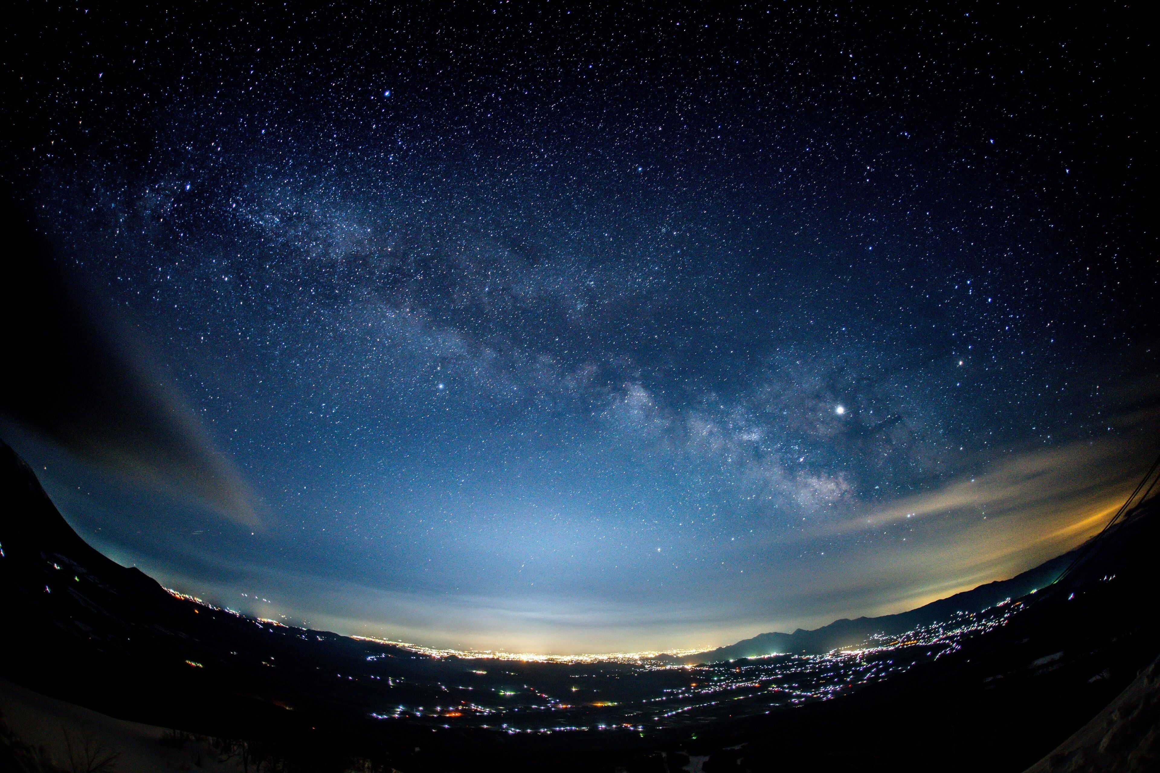 Céu noturno estrelado com a Via Láctea sobre uma paisagem urbana.
