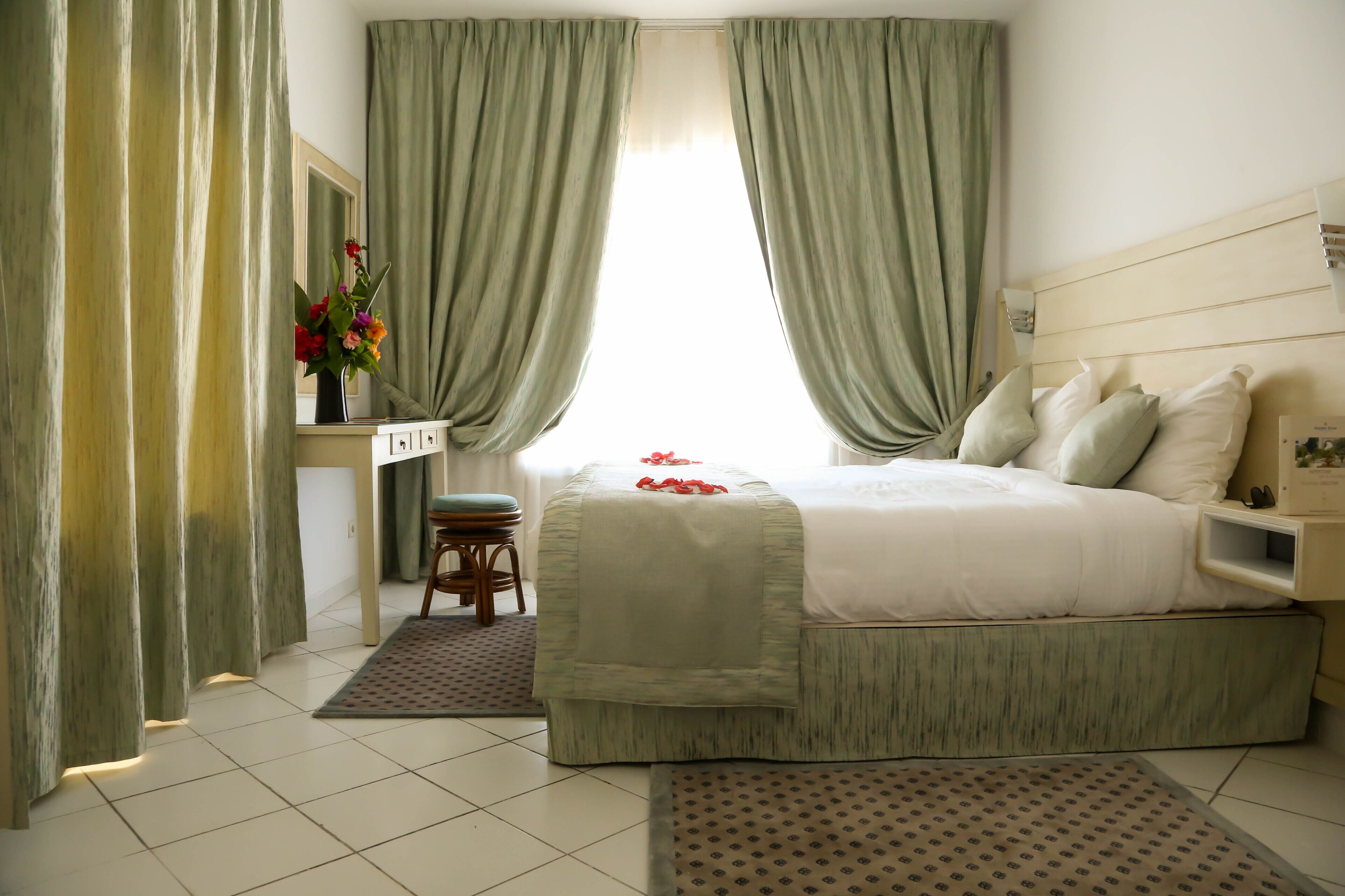 Quarto com cama, mesa de cabeceira, espelho, cômoda e janela com cortinas.