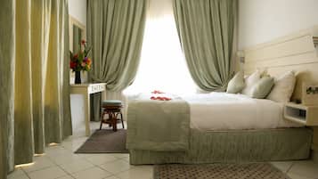 Quarto com cama, mesa de cabeceira, espelho, cômoda e janela com cortinas.