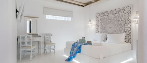 Quarto com cama, escrivaninha, duas cadeiras, ventilador de teto e painel decorativo na parede.